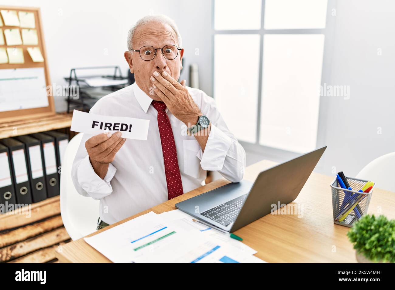 Senior business man holding fired banner at the office covering mouth ...