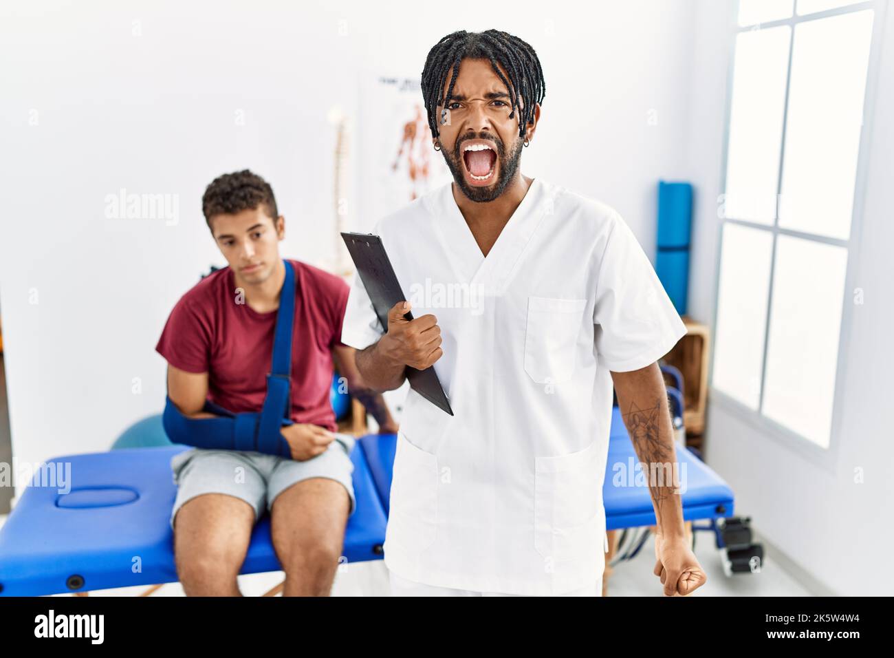 Young hispanic man working at pain recovery clinic with a man with ...