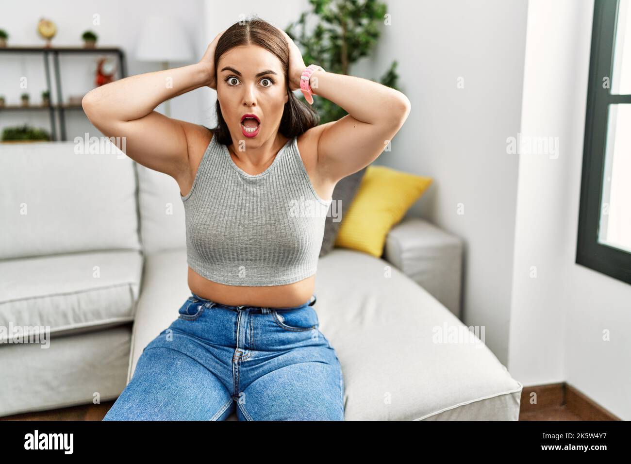 Young brunette woman sitting on the sofa at home crazy and scared with ...