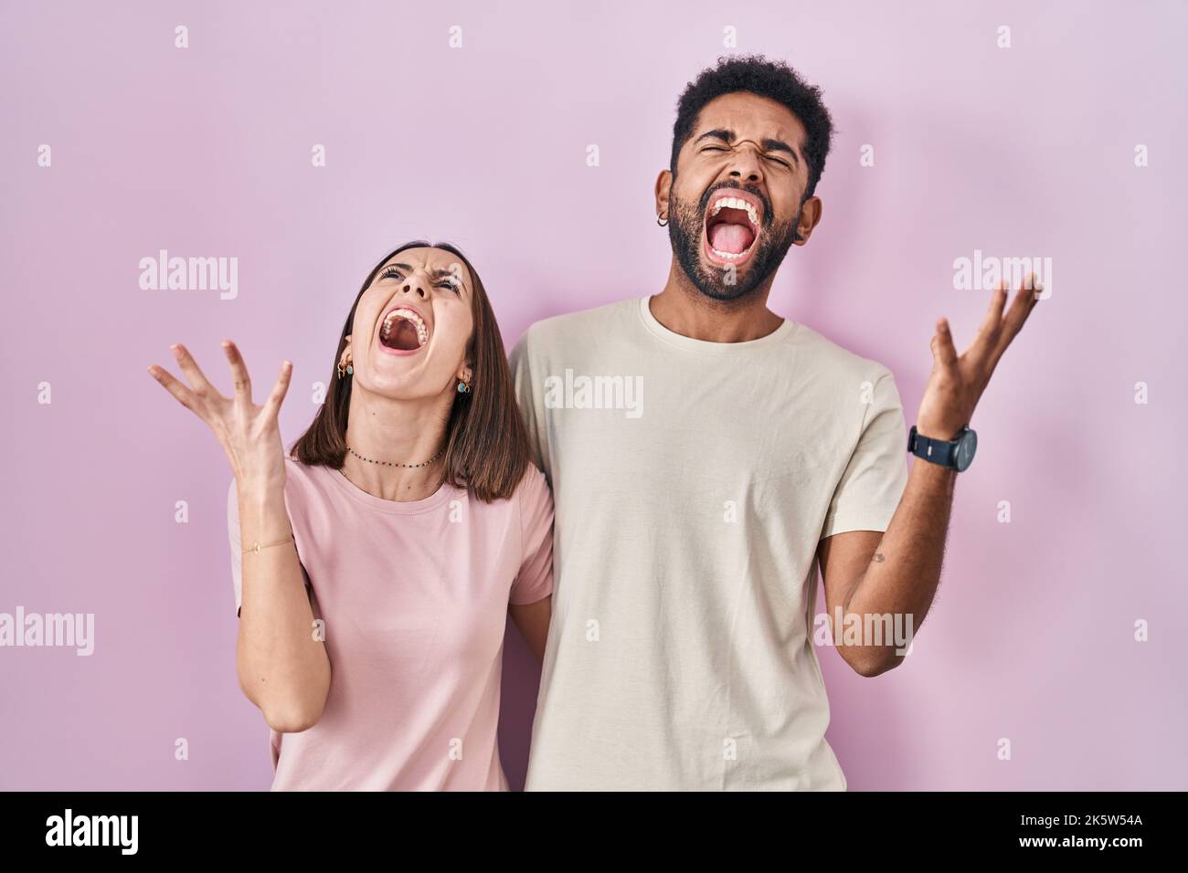 Young hispanic couple together over pink background crazy and mad ...