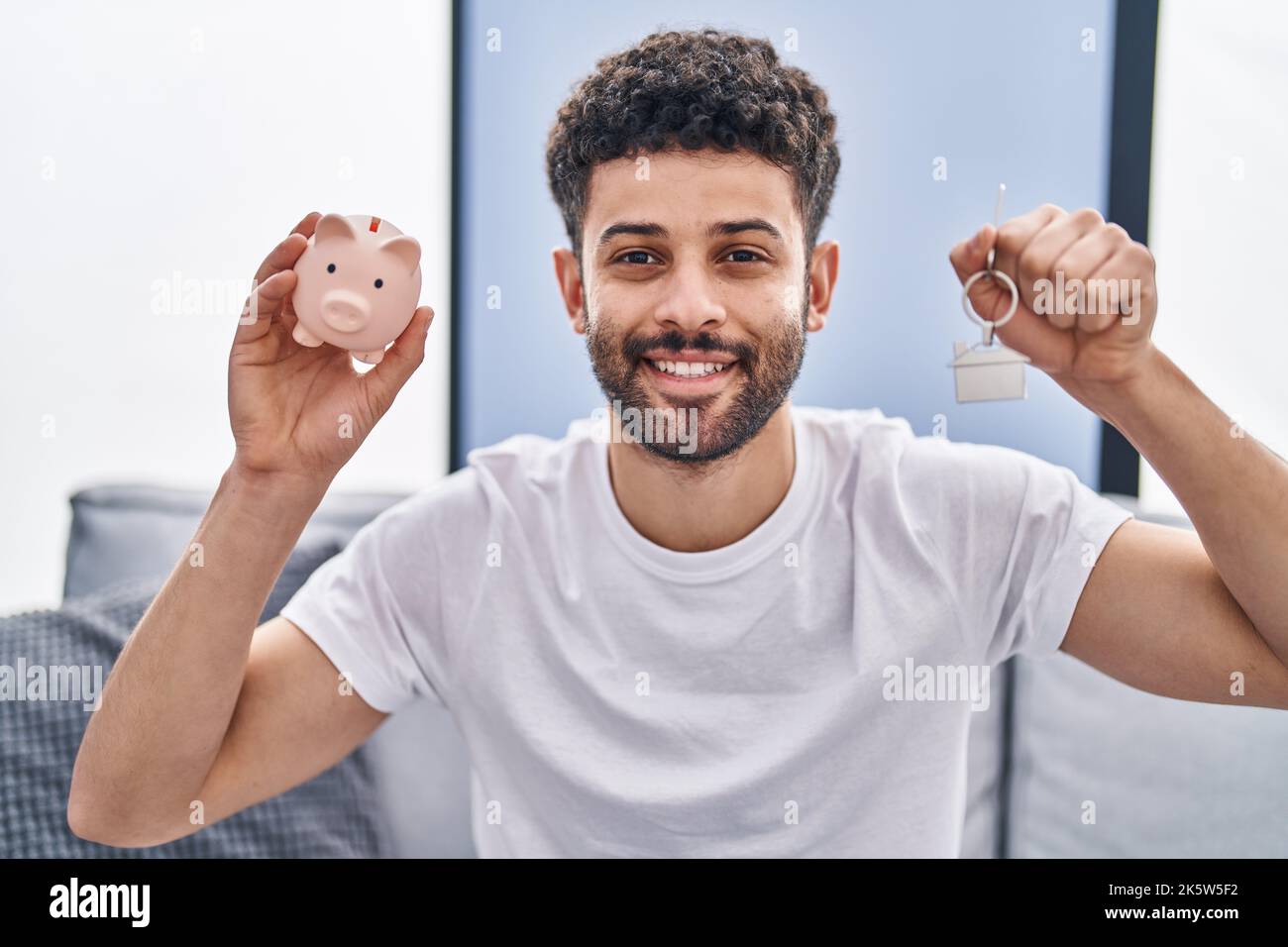 Arab man holding piggy bank and house keys smiling with a happy and ...