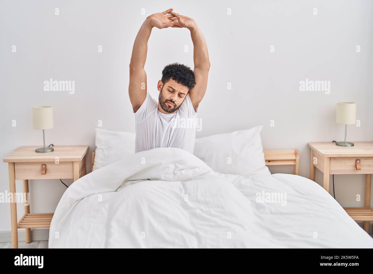 Young arab man waking up stretching arms at bedroom Stock Photo - Alamy