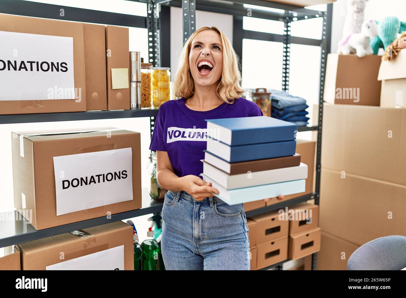 Beautiful blonde woman wearing volunteer t shirt holding books angry ...