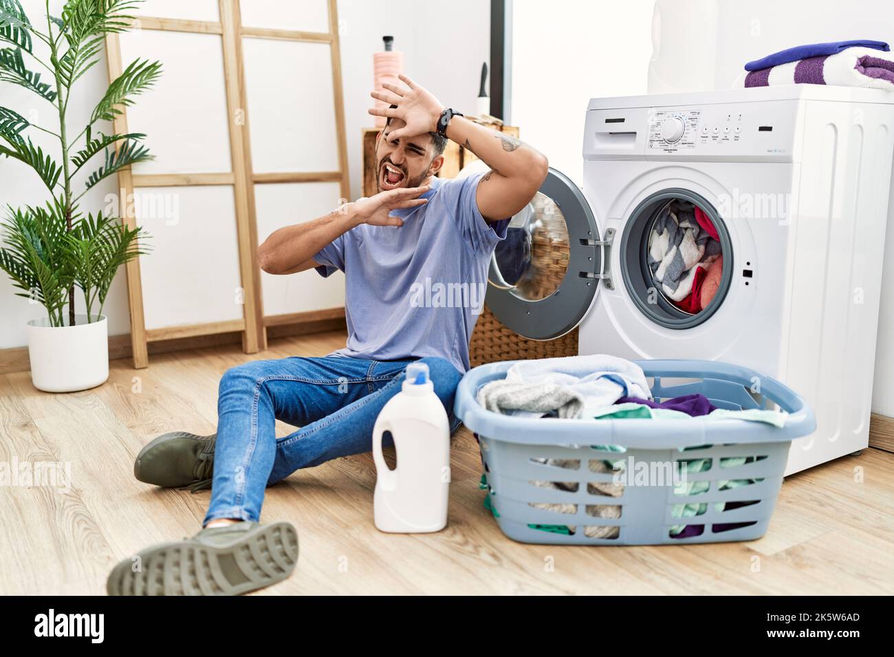 Young hispanic man putting dirty laundry into washing machine smiling ...