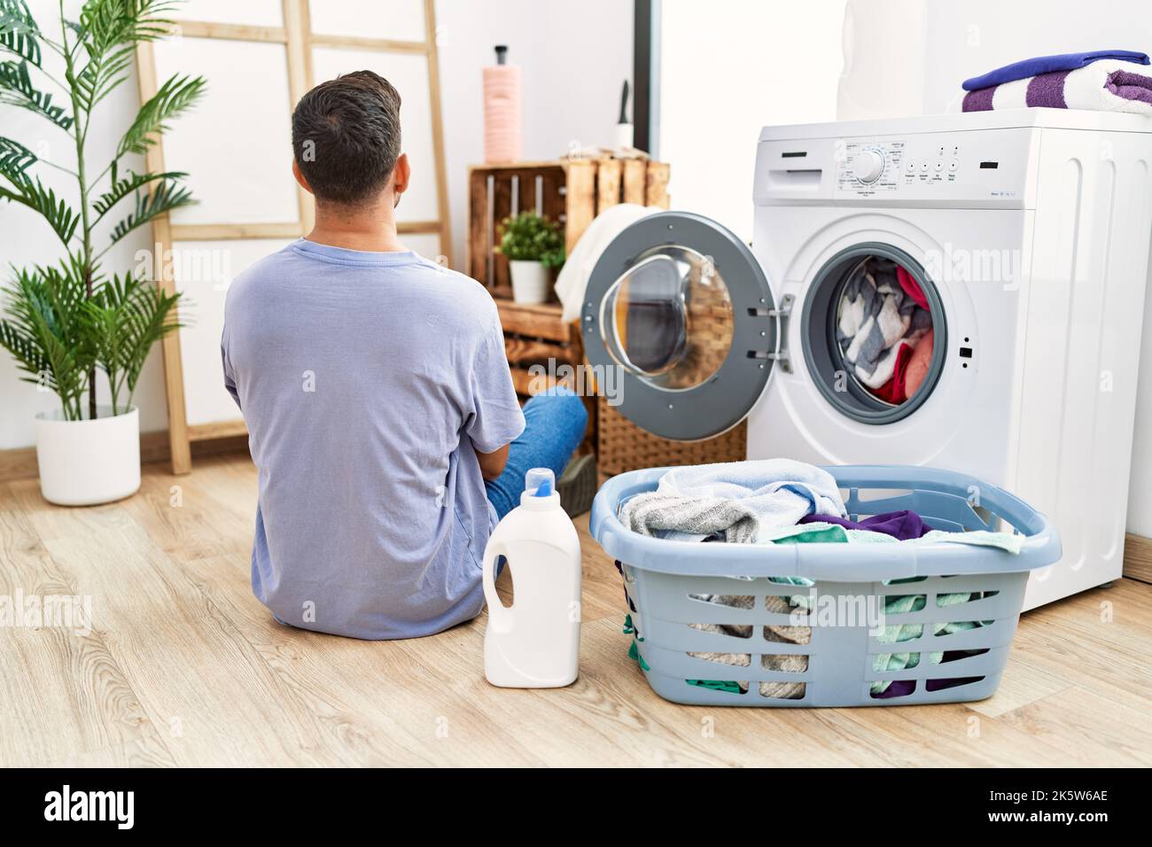Young hispanic man putting dirty laundry into washing machine standing ...