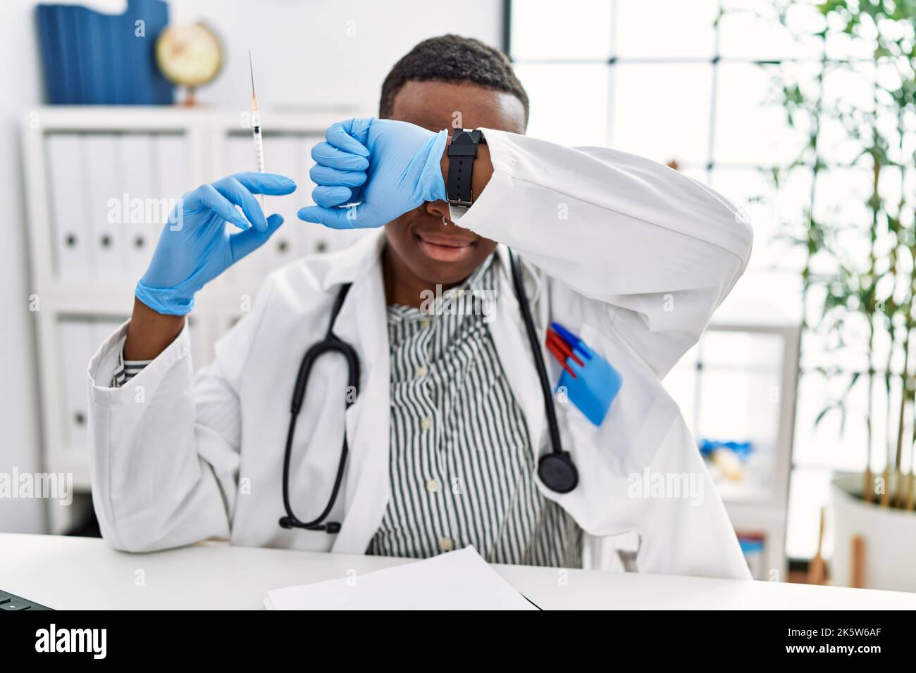 Young african doctor man holding syringe at the hospital smiling ...