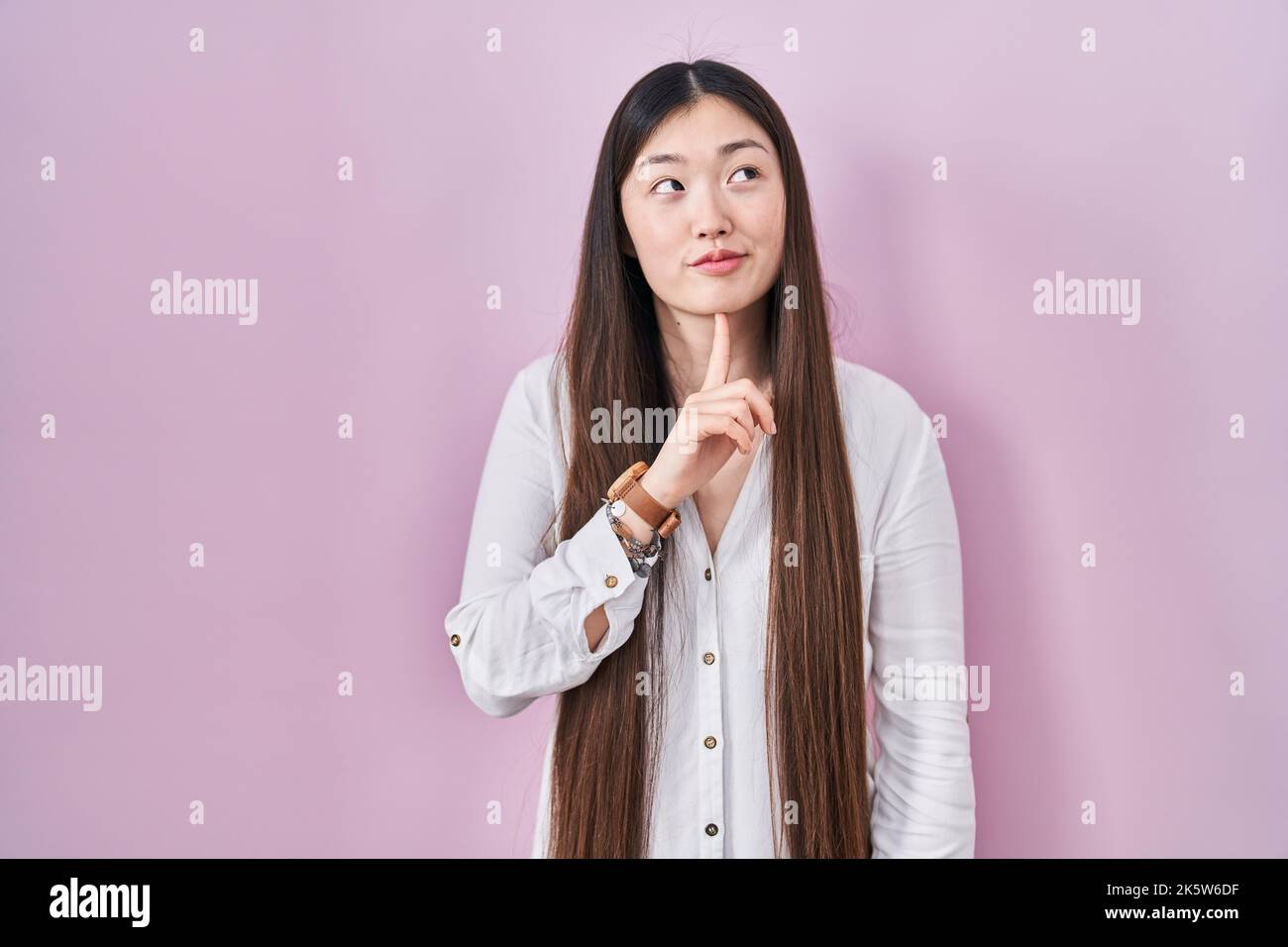Chinese young woman standing over pink background thinking concentrated ...