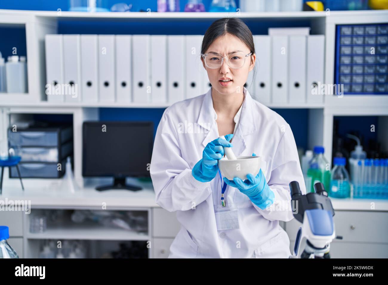 Chinese young woman working at scientist laboratory mixing clueless and ...