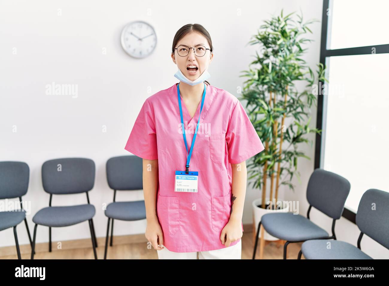 Young asian nurse woman at medical waiting room angry and mad screaming ...