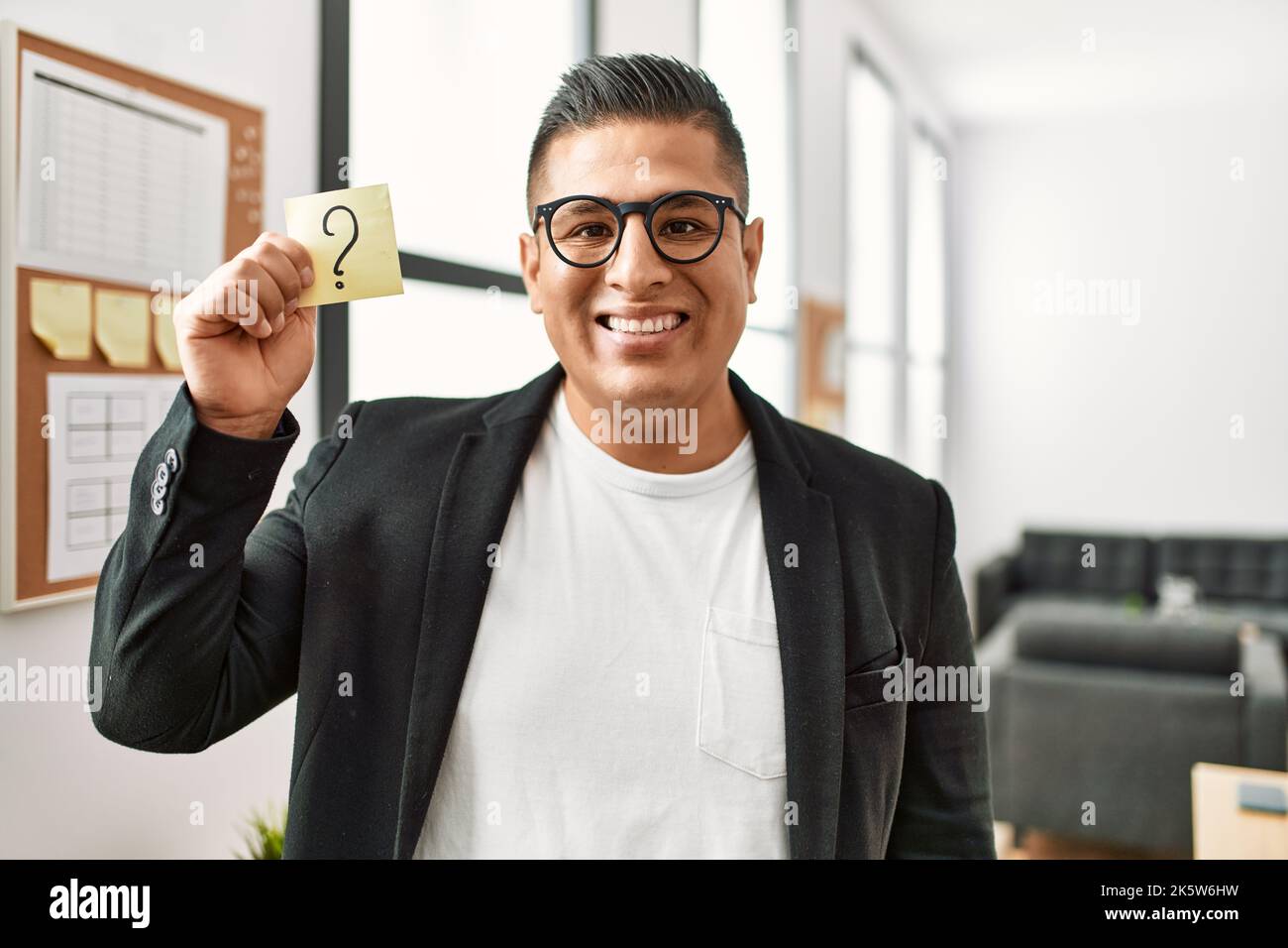 Young latin businessman smiling happy holding question mark reminder at ...