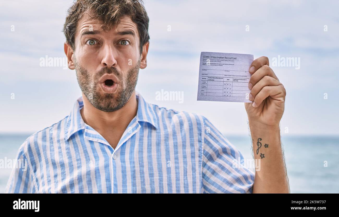 Young handsome man holding covid record card scared and amazed with ...