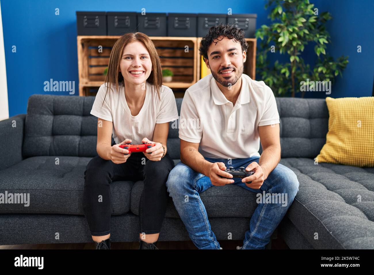 Young couple playing video game holding controller at home looking ...