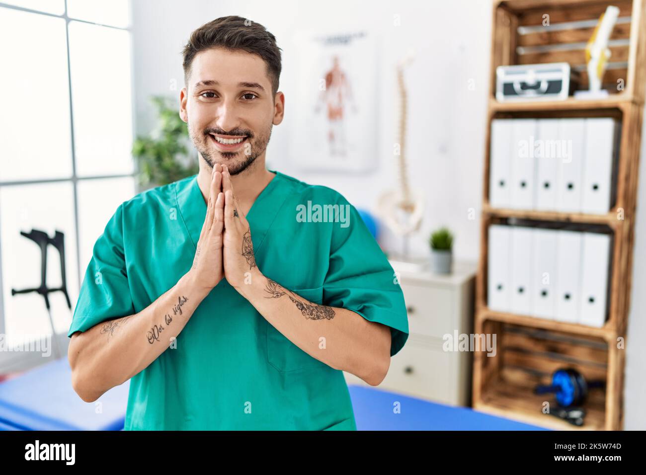 Young physiotherapist man working at pain recovery clinic praying with ...