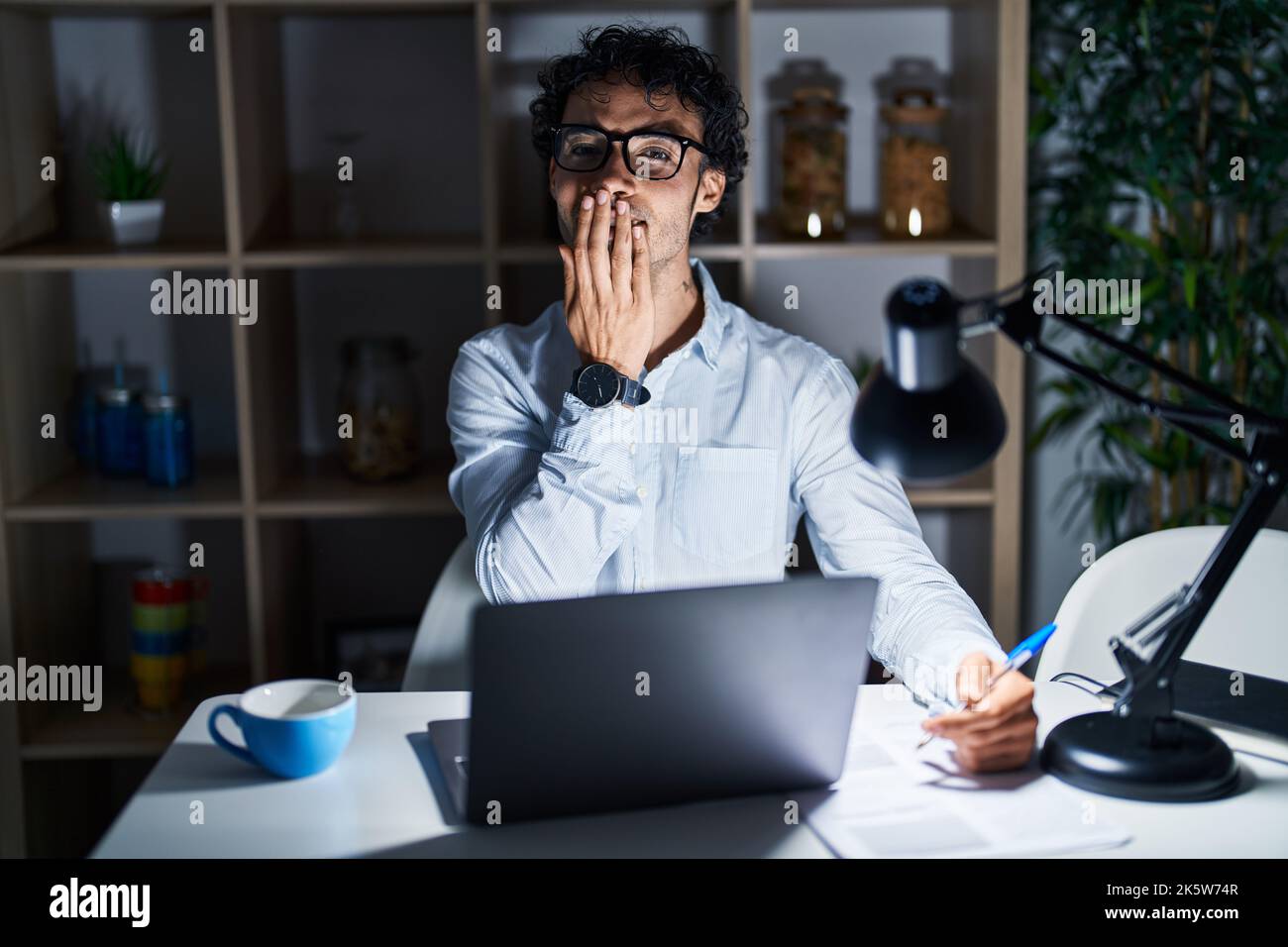 Hispanic man working at the office at night laughing and embarrassed ...