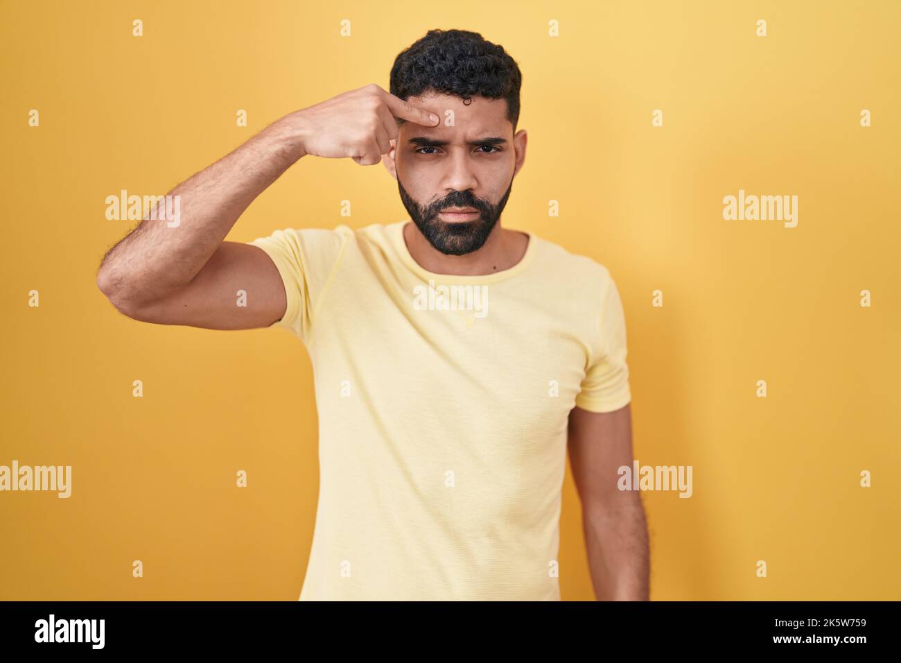 Hispanic man with beard standing over yellow background pointing ...