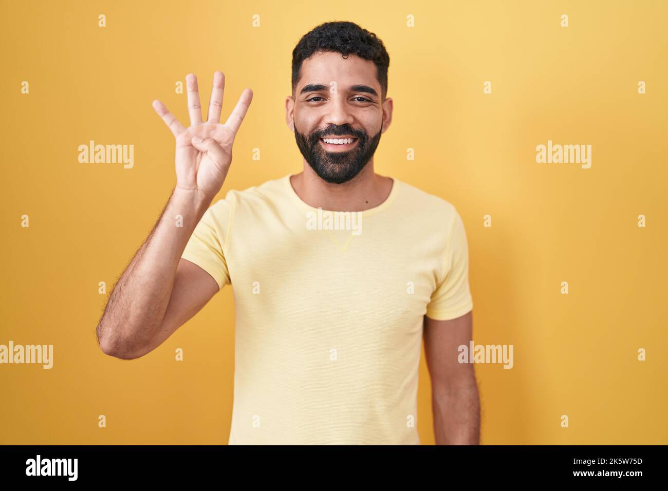 Hispanic man with beard standing over yellow background showing and ...