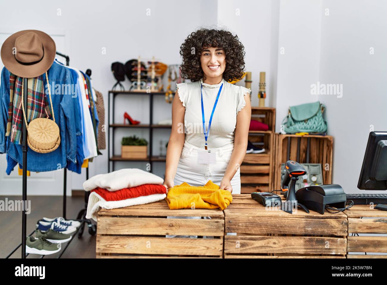 Young middle east shopkeeper woman smiling happy folding sweater at ...