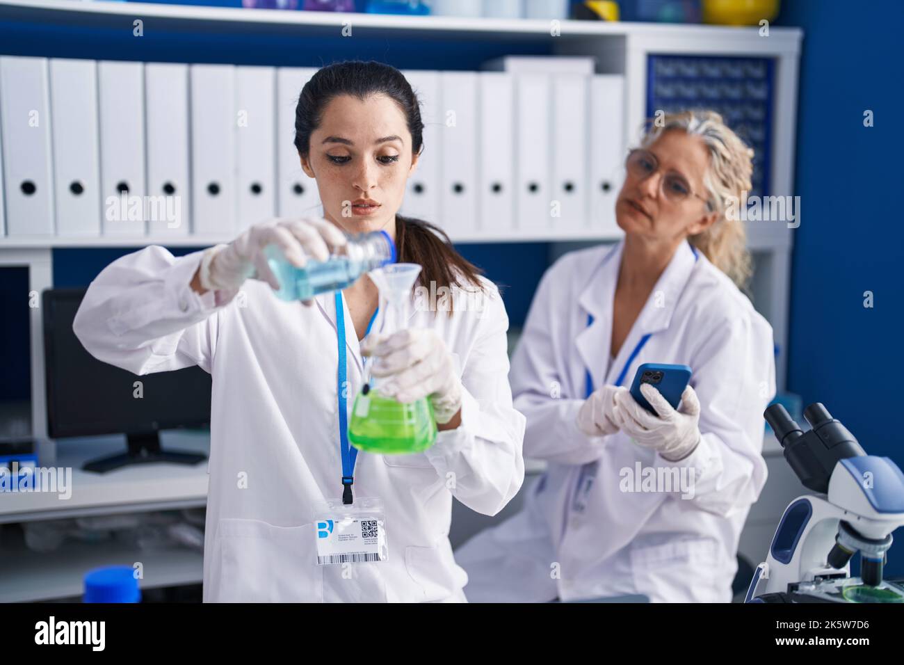 Two women scientists using smartphone and measuring liquid at ...