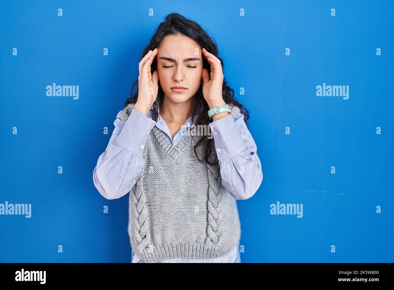 Young brunette woman standing over blue background with hand on head ...