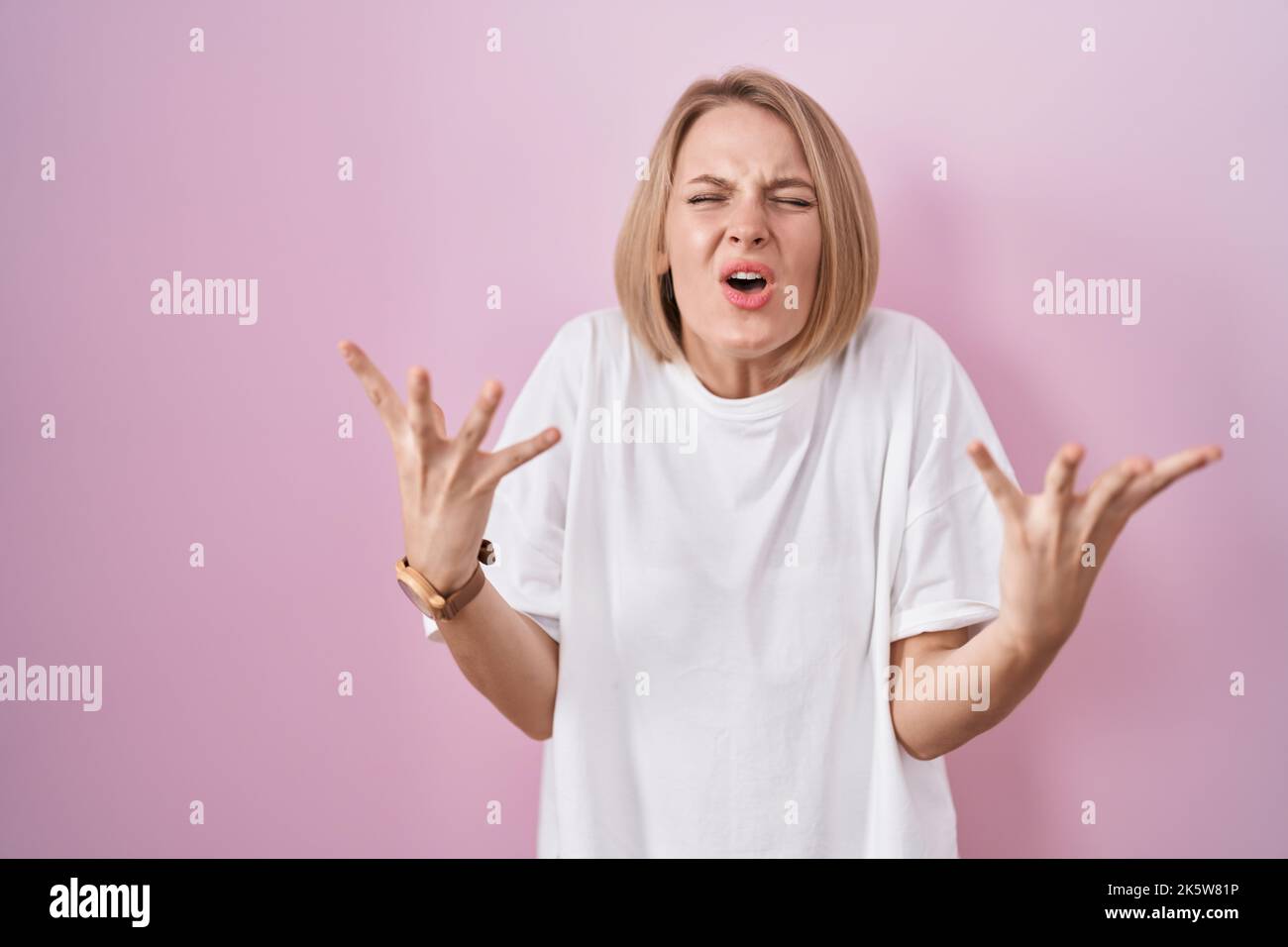Young caucasian woman standing over pink background crazy and mad ...