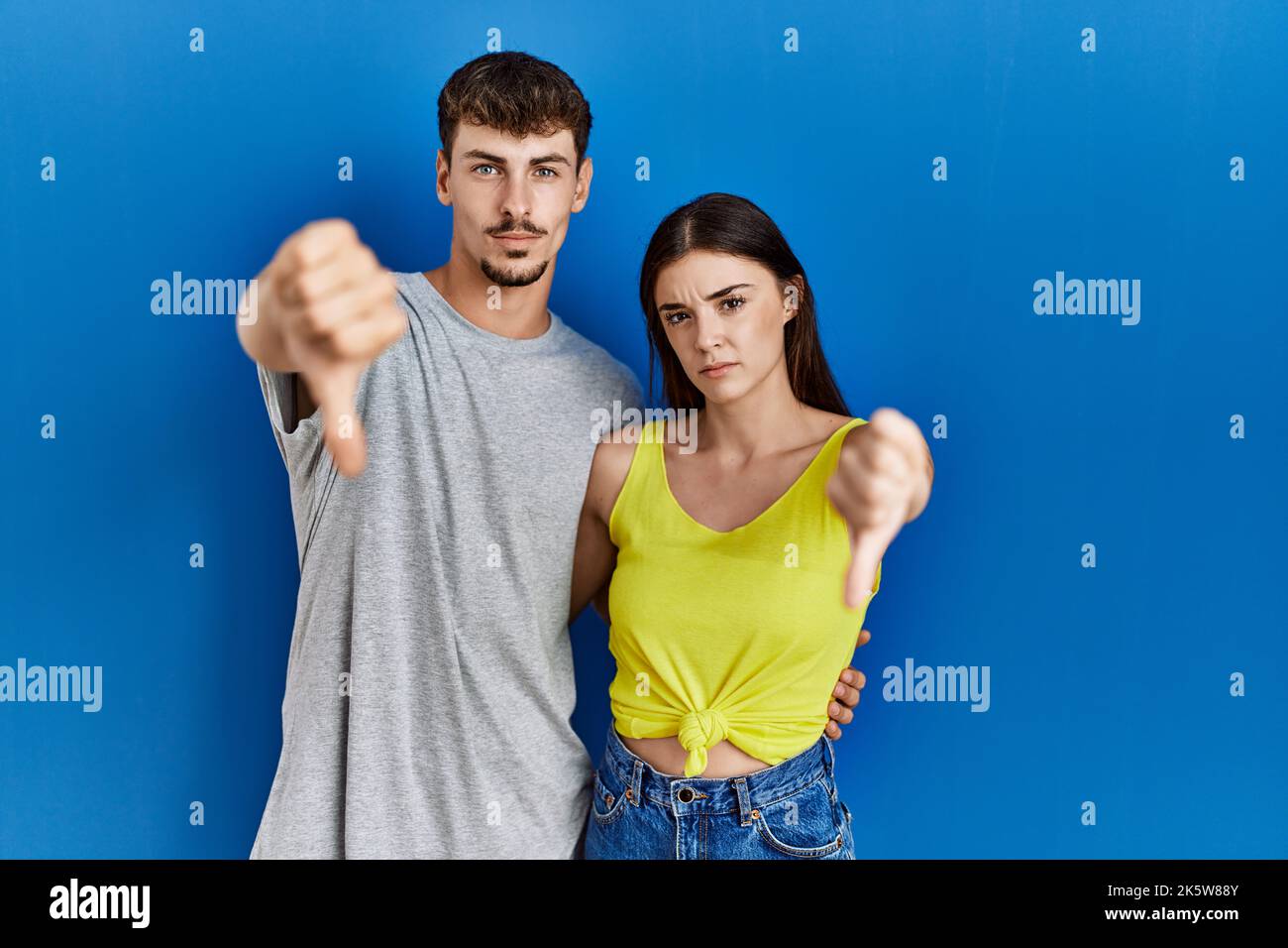 Young hispanic couple standing together over blue background looking ...