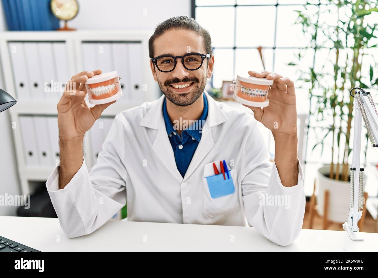 Young hispanic dentist man holding denture with orthodontic braces ...