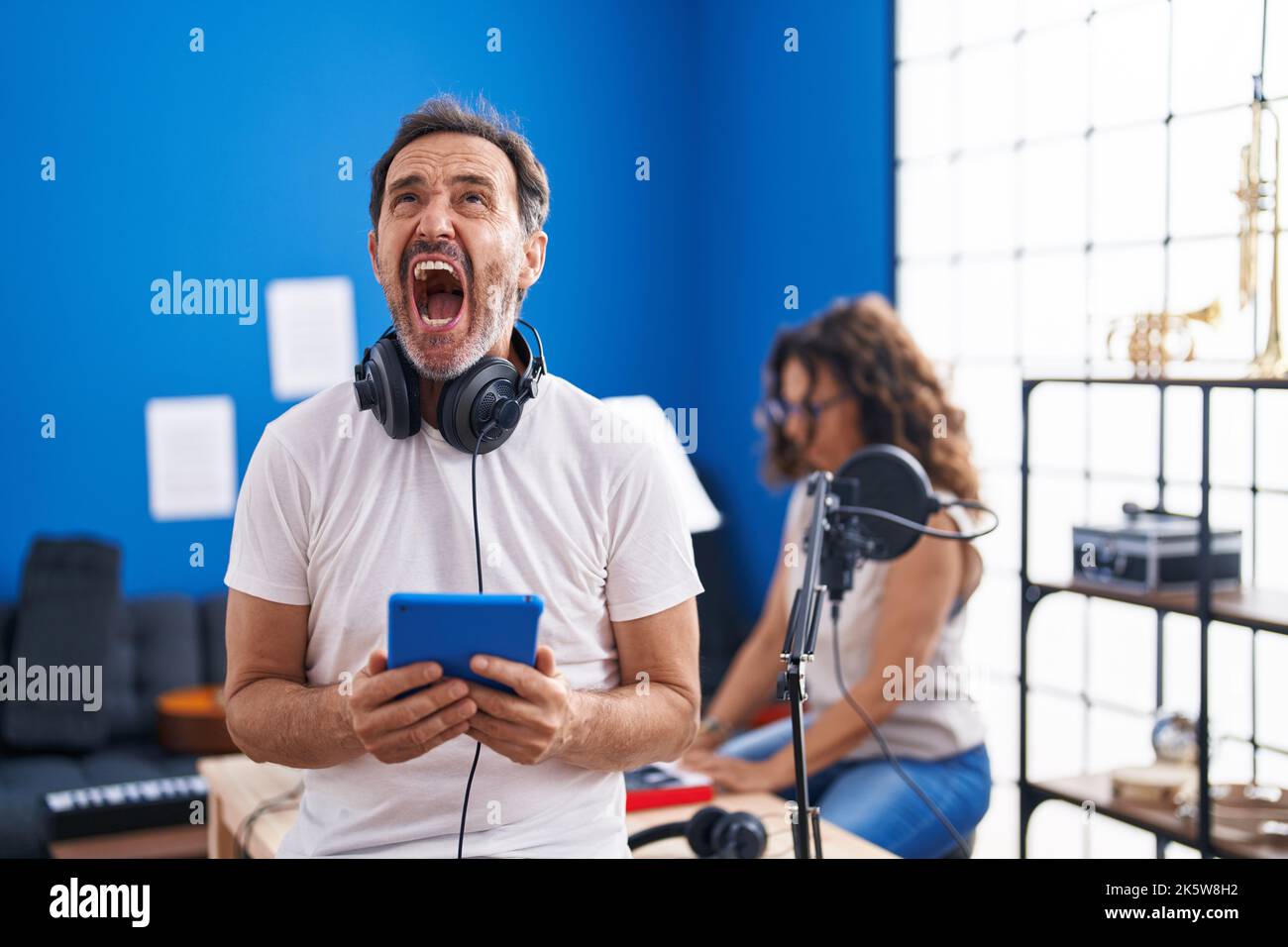 Middle age hispanic man at music studio using tablet angry and mad ...