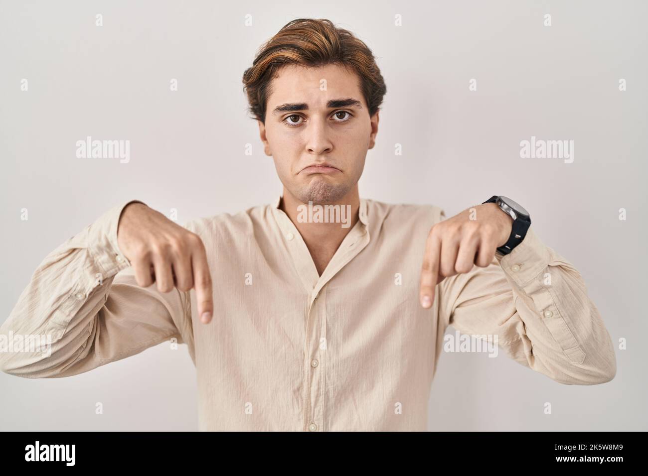 Young man standing over isolated background pointing down looking sad ...