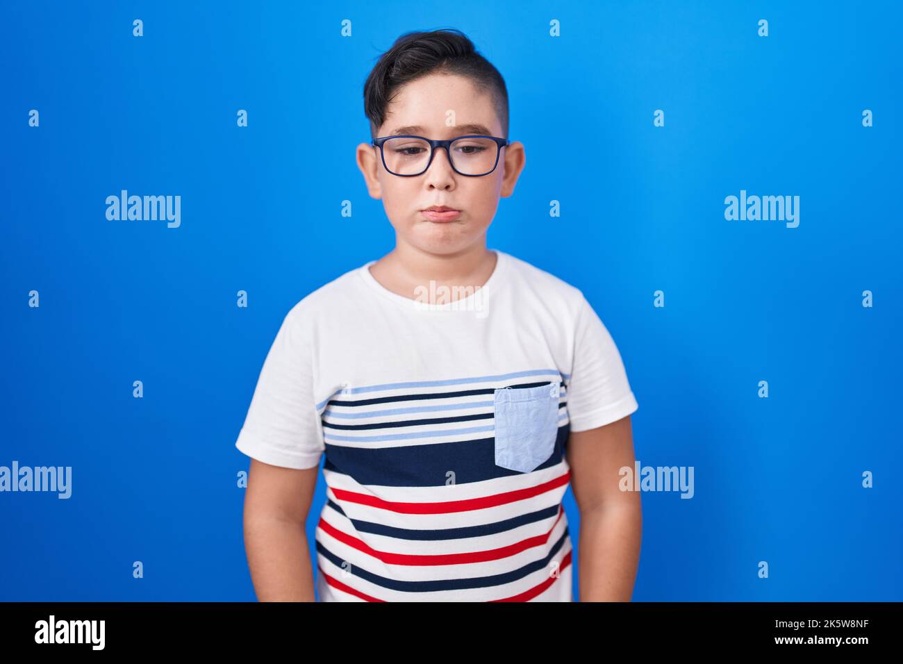 Young hispanic kid standing over blue background depressed and worry ...