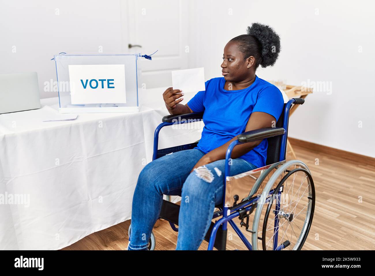 Young african woman sitting on wheelchair voting putting envelop in ...