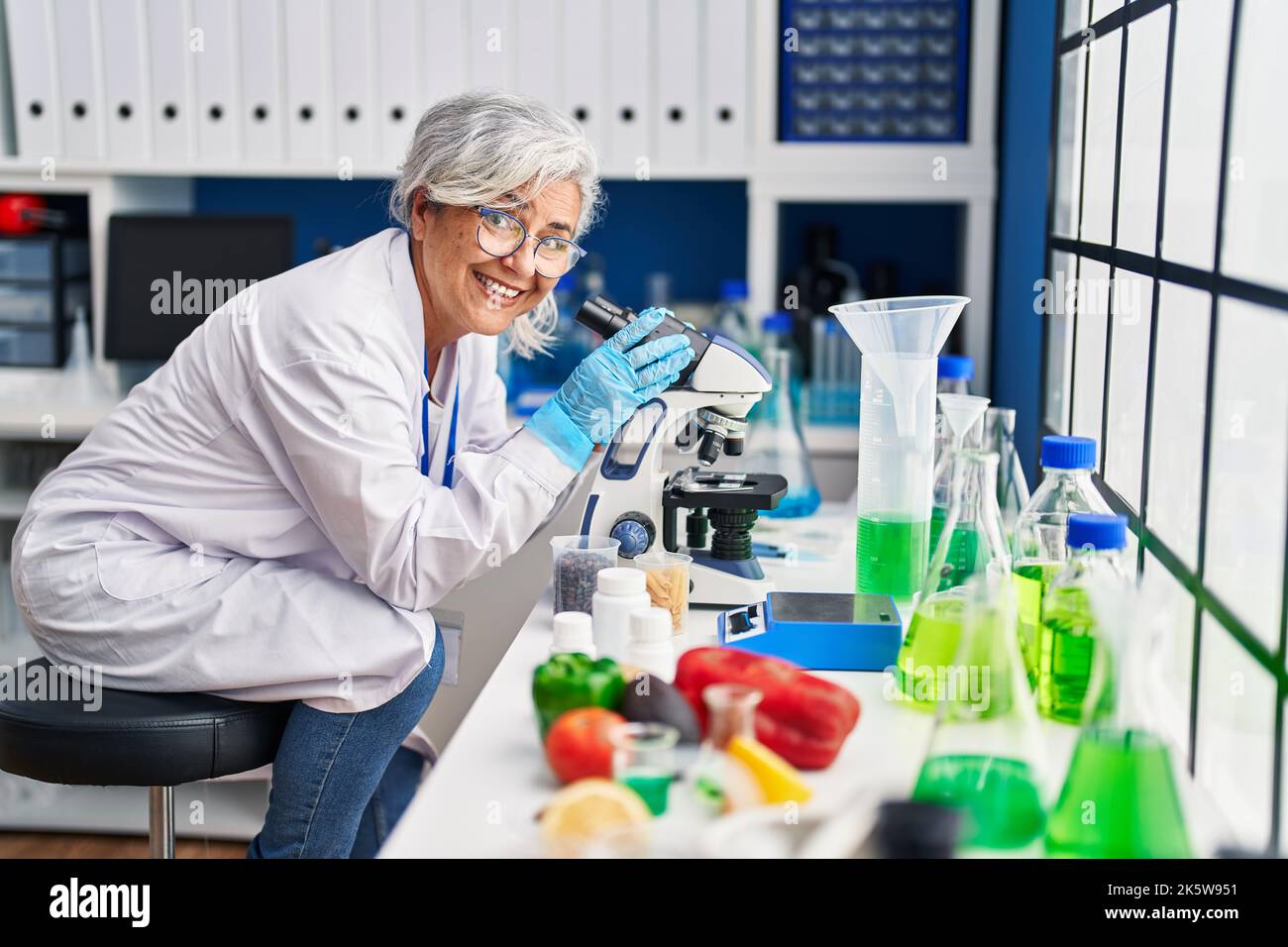 Middle age woman wearing scientist uniform using microscope at ...
