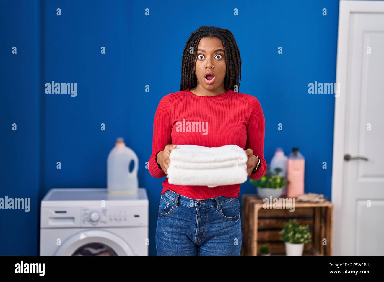 Young african american with braids holding clean laundry in shock face ...