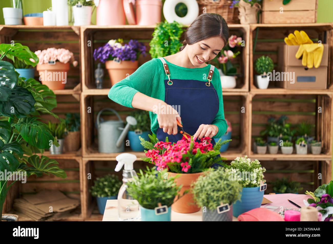 Young beautiful hispanic woman florist cutting plants at flower shop ...