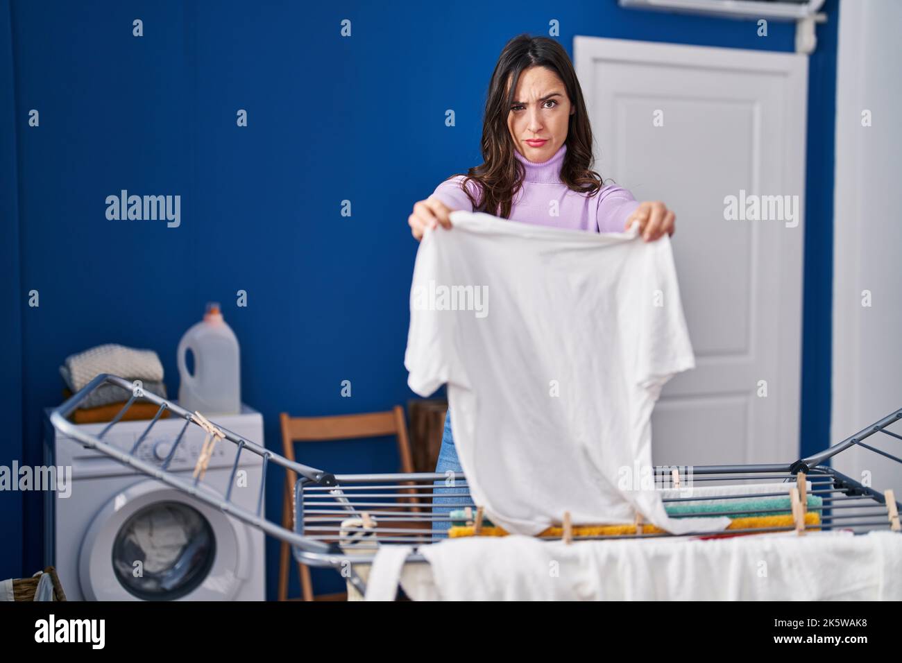 Young brunette woman hanging clothes at clothesline skeptic and nervous ...