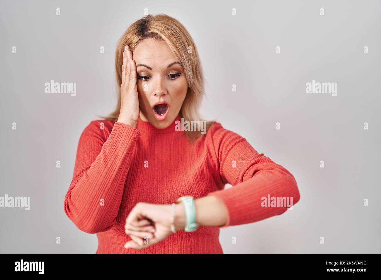 Blonde woman standing over isolated background looking at the watch ...