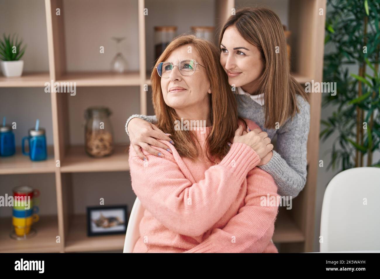 Mother and daughter hugging each other sitting on desk at home Stock Photo - Alamy