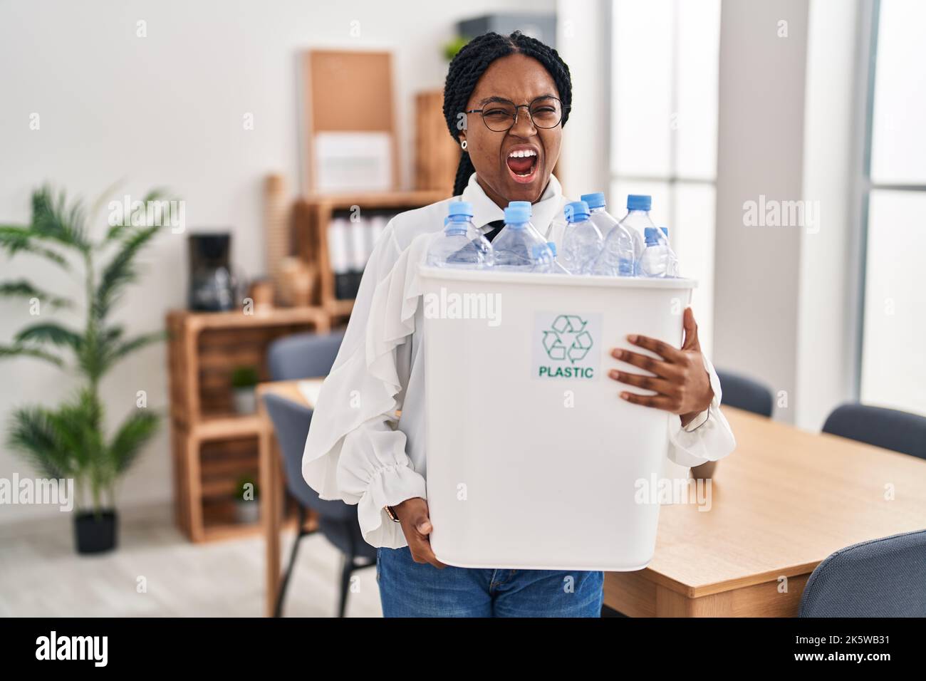 African american woman working at the office holding plastic bottle for ...