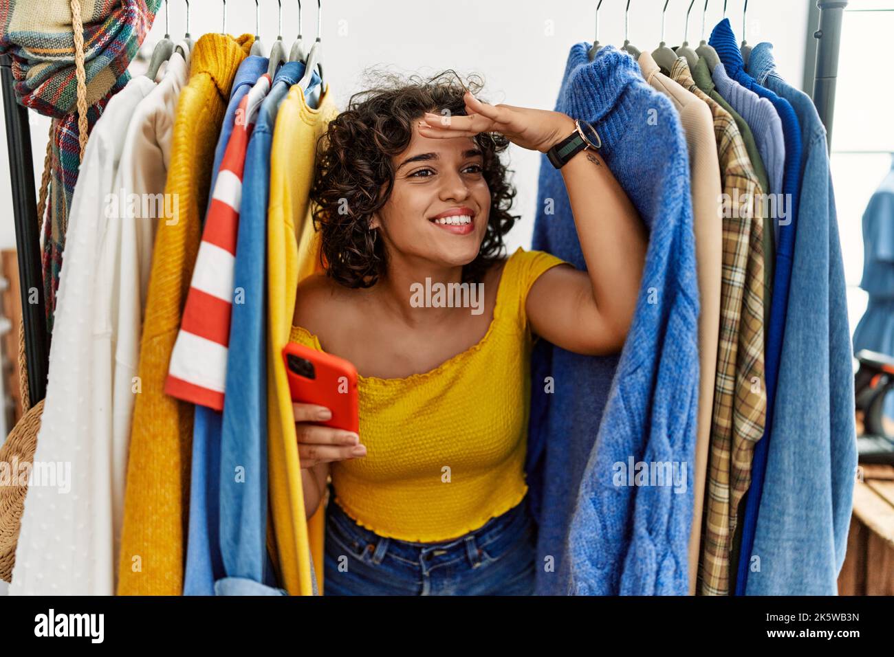 Young hispanic woman searching clothes on clothing rack using ...