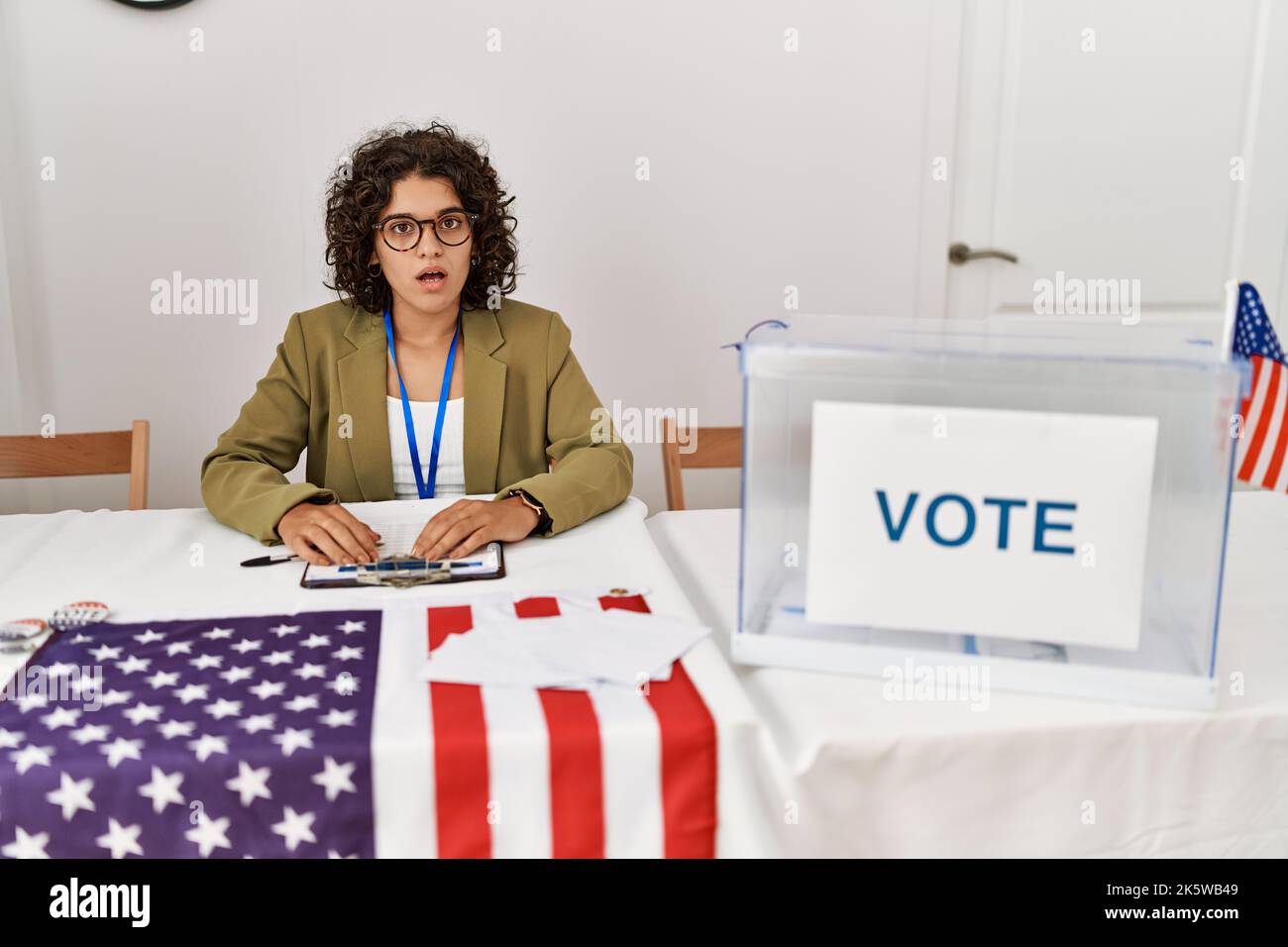 Young hispanic woman at political election sitting by ballot afraid and ...