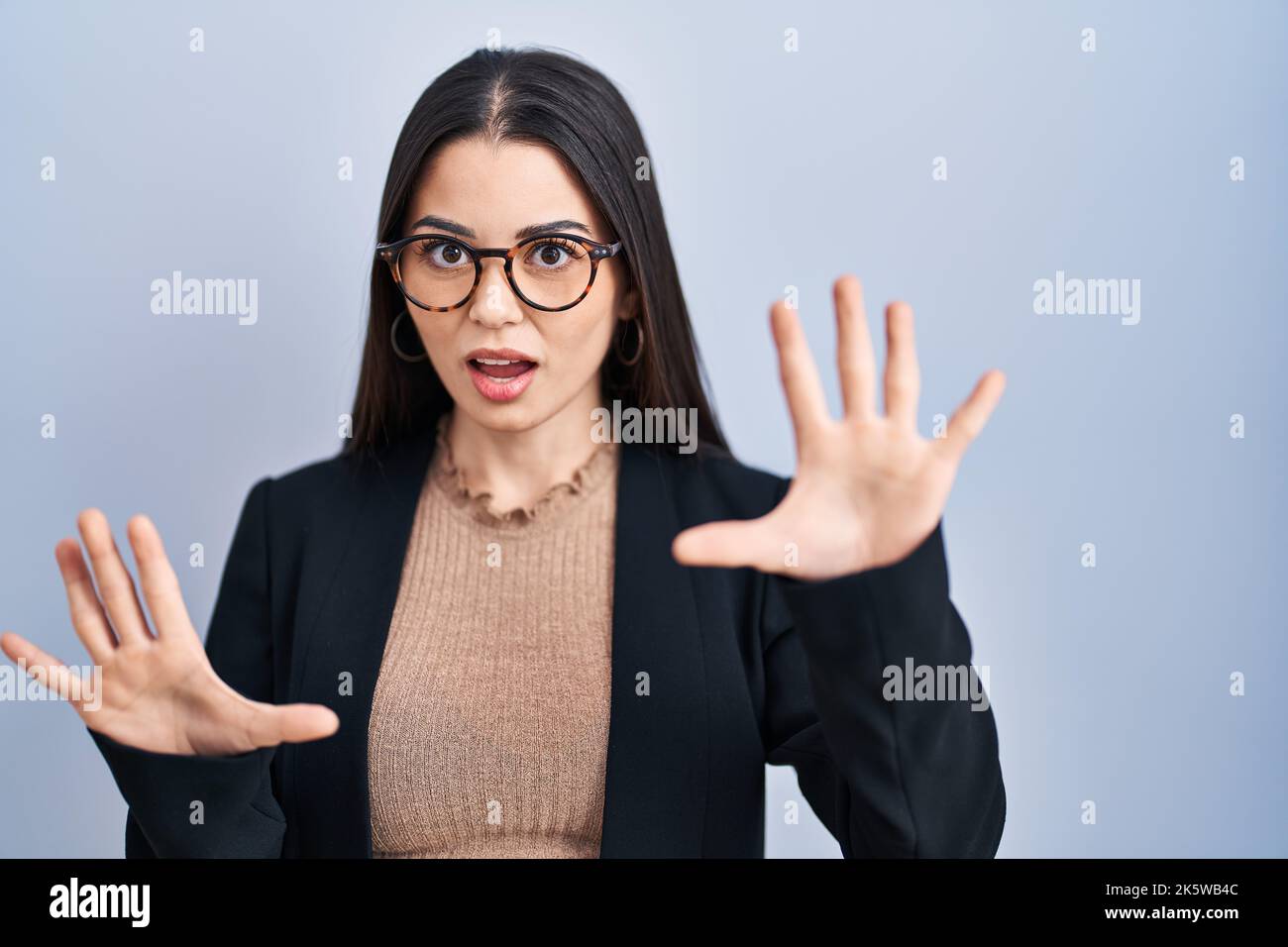 Young brunette woman standing over blue background afraid and terrified ...