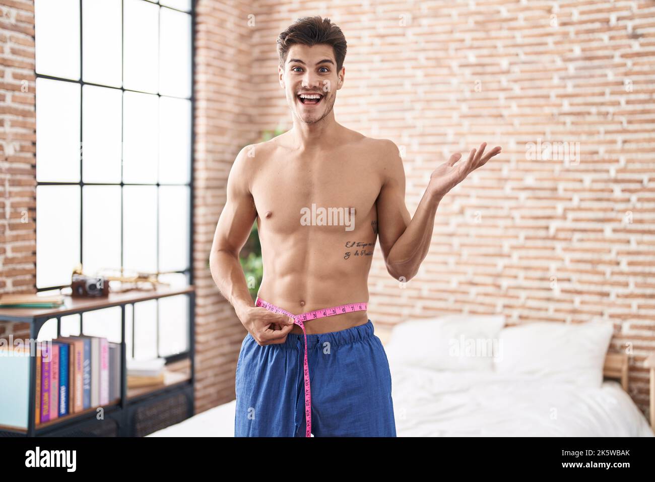 Young hispanic man using tape measure measuring waist celebrating ...