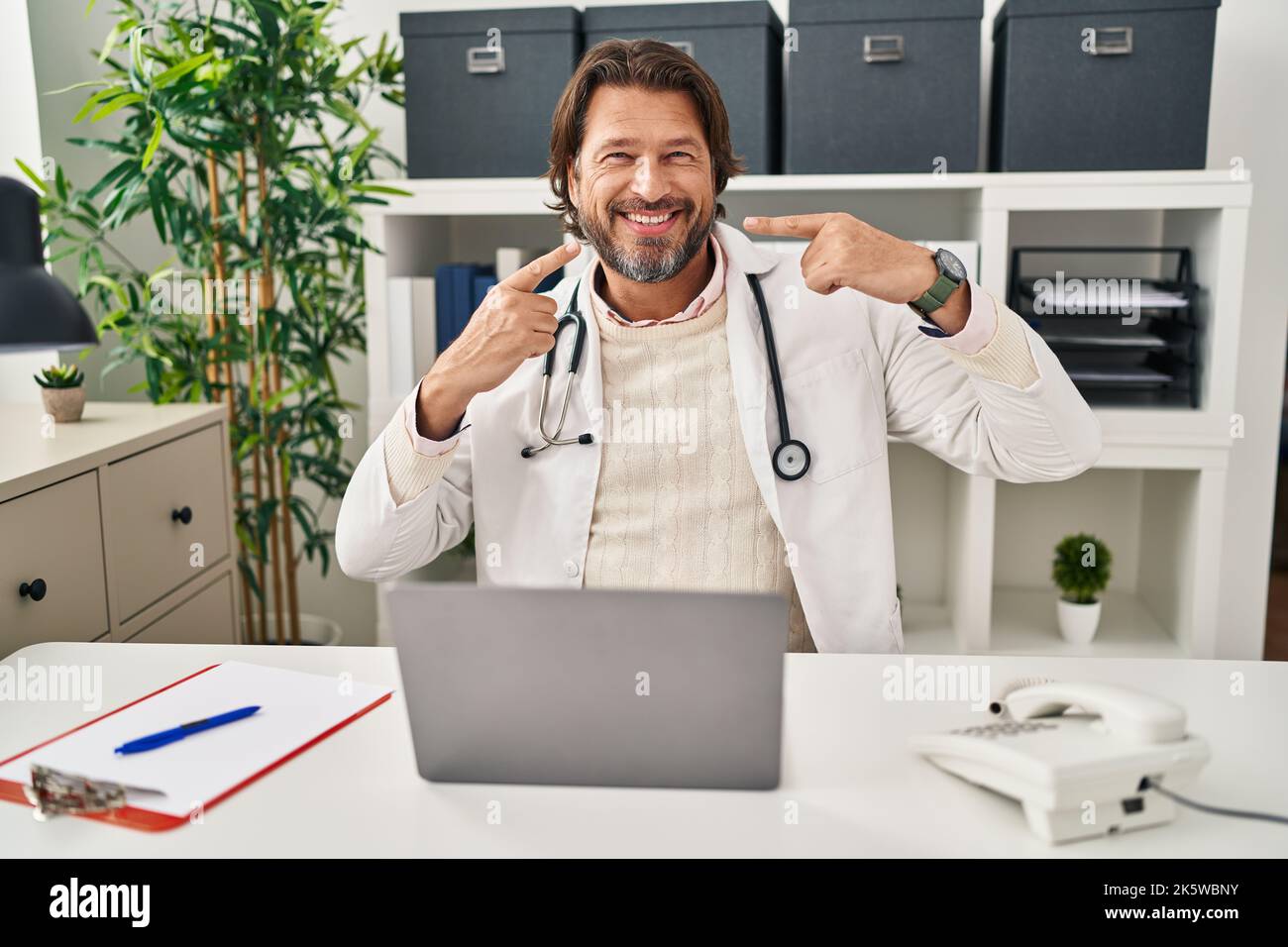 Handsome middle age doctor man working at the clinic smiling cheerful ...