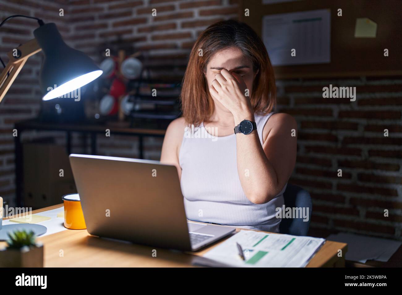 Brunette woman working at the office at night tired rubbing nose and ...