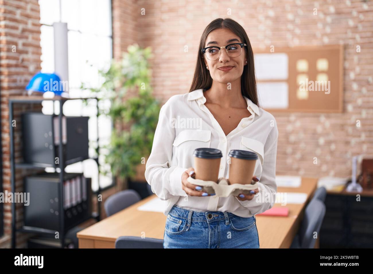 Young brunette woman working at the office holding take away coffee ...