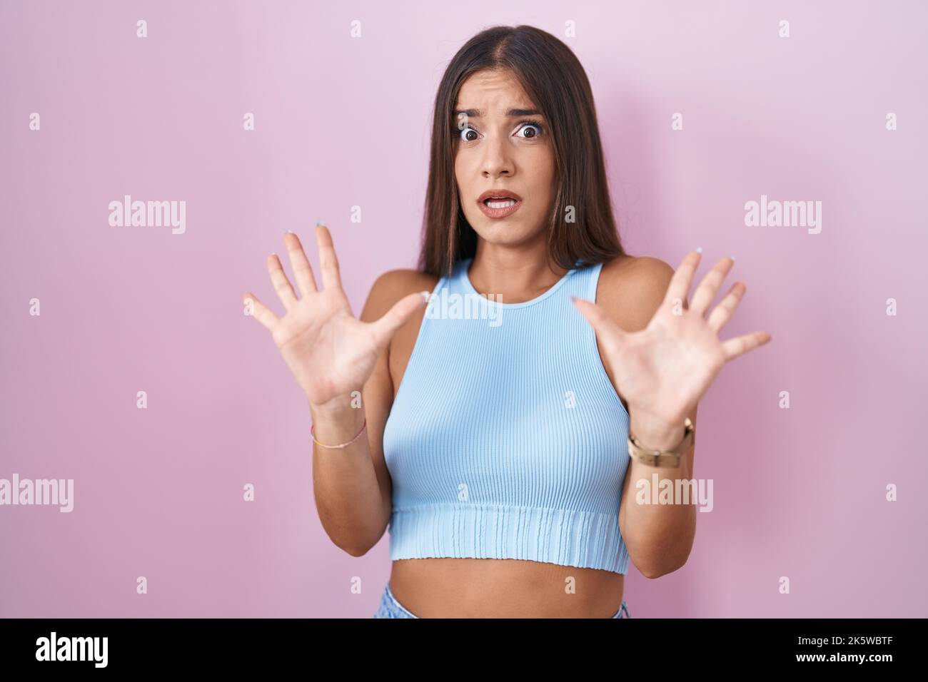 Young brunette woman standing over pink background afraid and terrified ...