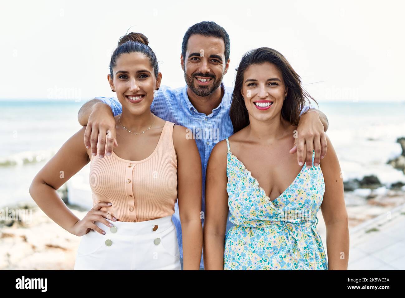 Three young hispanic friends smiling happy and hugging at the beach ...