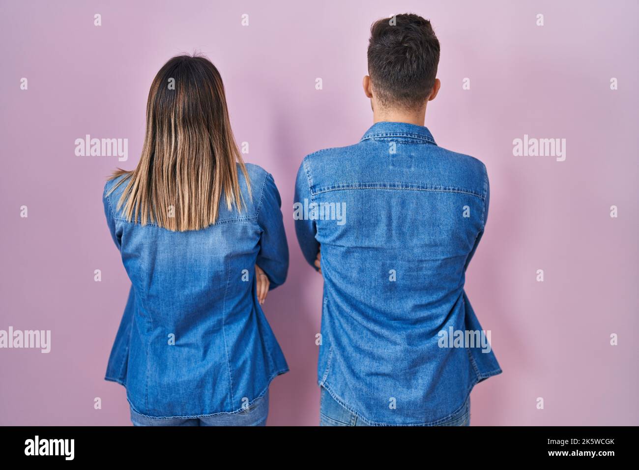 Young hispanic couple standing over pink background standing backwards ...
