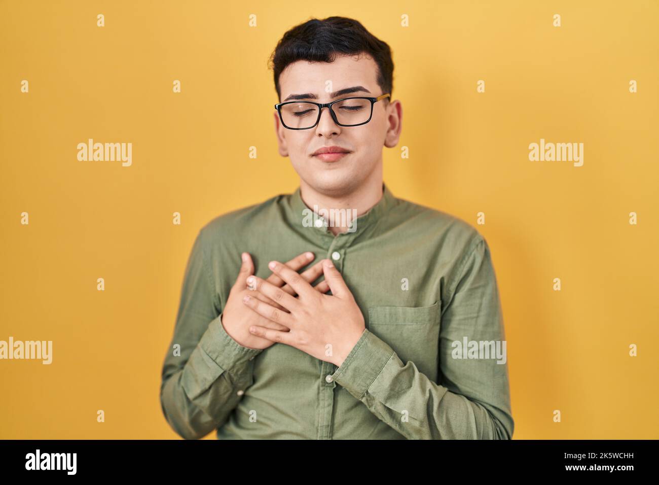Non binary person standing over yellow background smiling with hands on ...