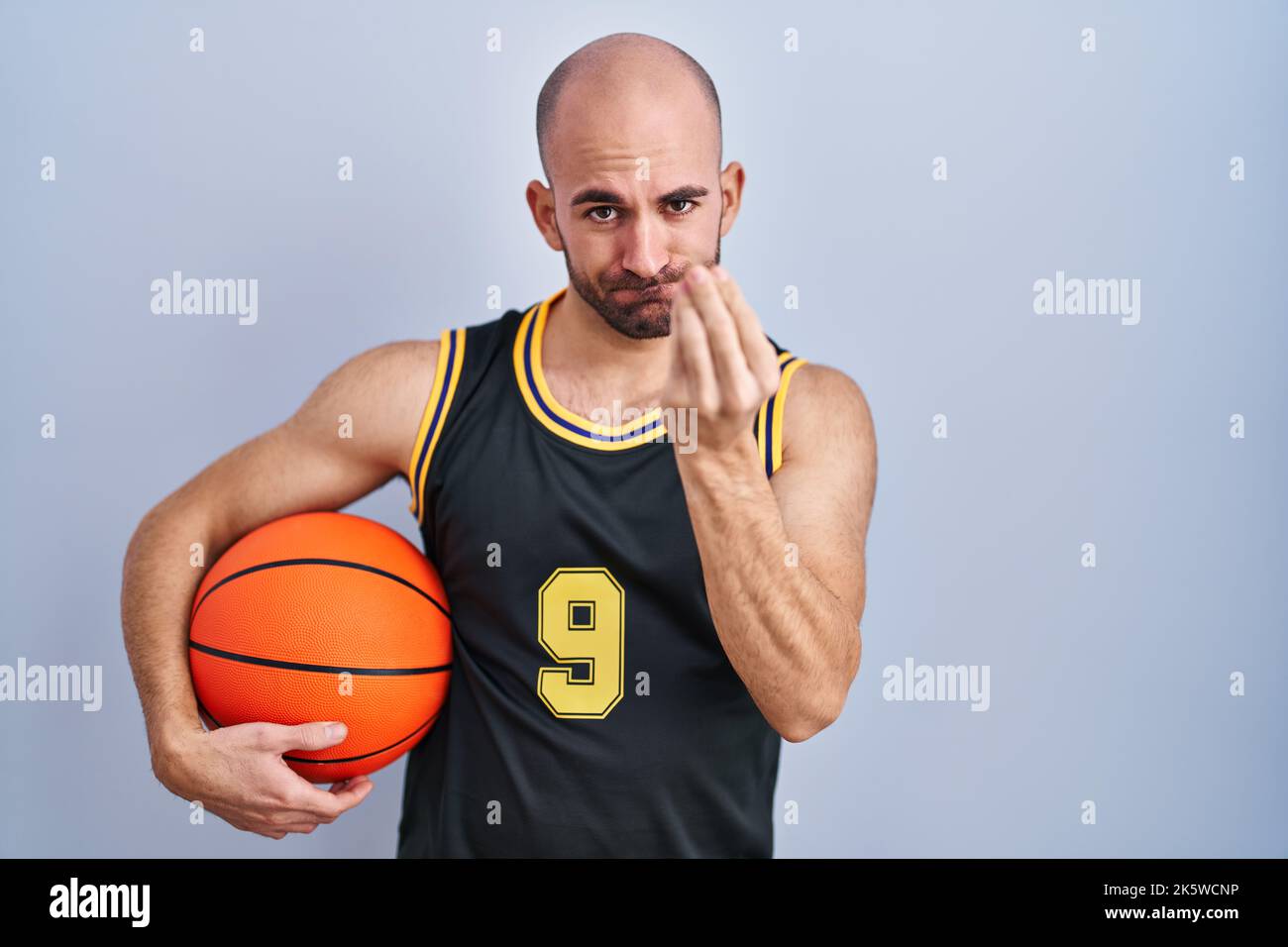 Young bald man with beard wearing basketball uniform holding ball doing ...