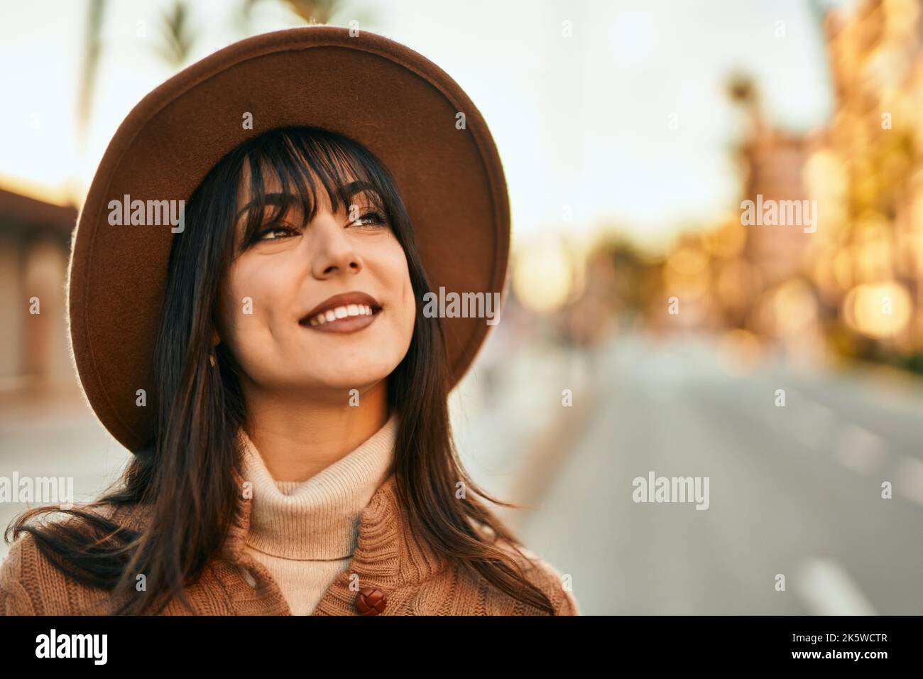 Brunette woman wearing winter hat smiling outdoors at the city on ...